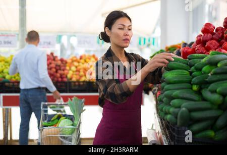 Supermarket worker putting cucumber on counter Stock Photo - Alamy