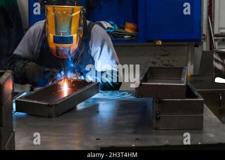 Professional welder performs work with metal parts in factory, sparks ...