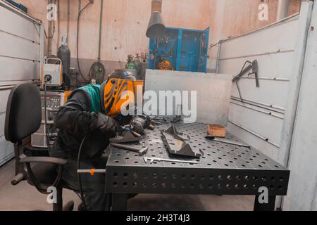 Professional welder performs work with metal parts in factory, sparks ...