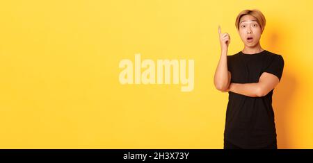 Handsome hipster man standing raising hands in the air in a yellow ...
