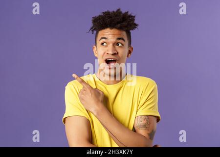 Portrait of impressed guy pointing finger left, showing smth shocking ...