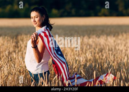 Woman with American flag in wheat field at sunset. 4th of July ...