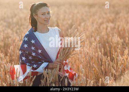 Woman with American flag and with a sheaf of ears in wheat field at ...