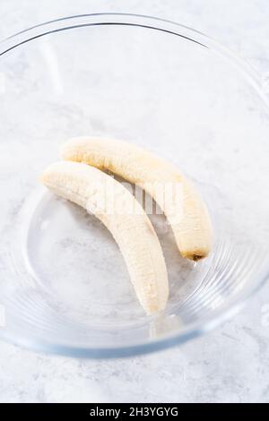Smashing riped bananas in a glass mixing bowl to prepare coconut banana ...