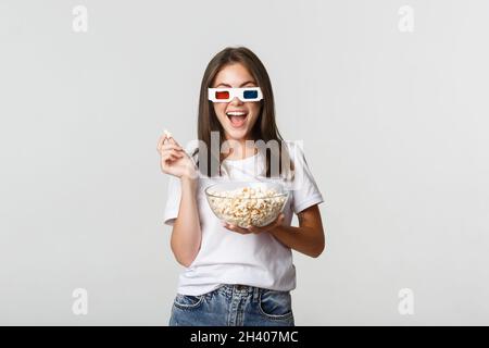 Girl eating popcorn, smiling amused as staring at large screen watching ...