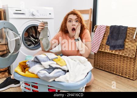 Young redhead woman putting dirty laundry into washing machine pointing ...