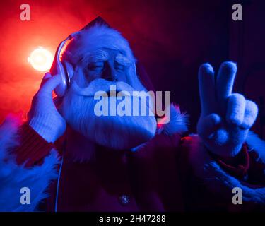 Santa claus listens to music with headphones at a party. Blue red neon ...