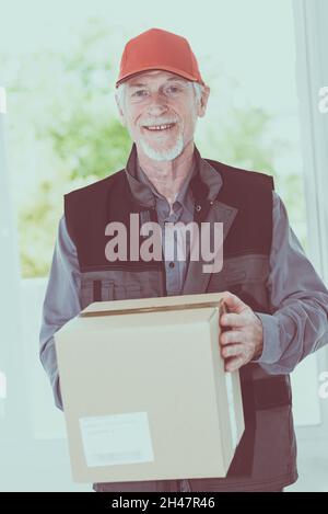 Portrait of smiling senior deliverer holding a package; panoramic ...