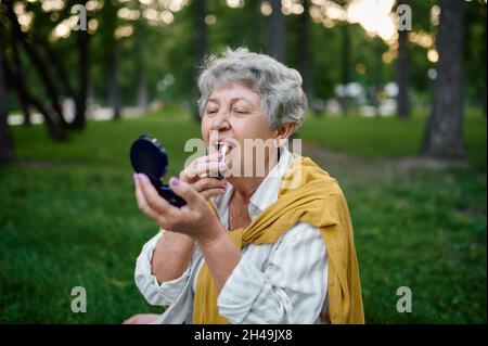 Pretty granny does makeup in summer park, back to youth. Aged people ...