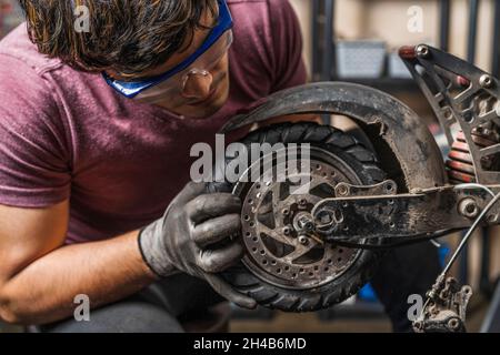 Mechanic with safety goggles putting the wheel of an electric scooter ...