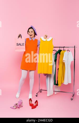 amazed woman with shopping bag near clothes and phone holder with ...