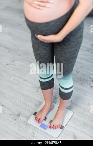 Young woman measuring her pregnant weight standing on scales ...
