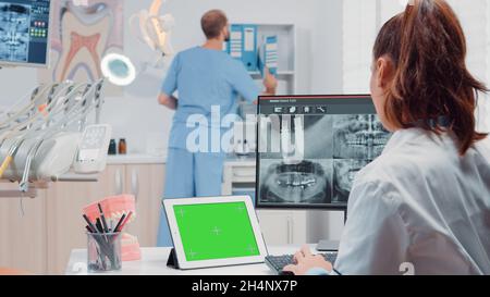 Dentist working with horizontal green screen on monitor at desk while ...