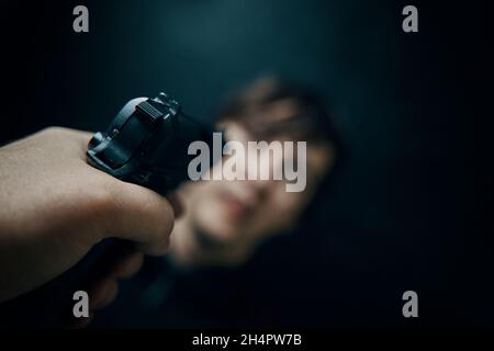 First person view of gun aimed at young man on dark background. POV of ...