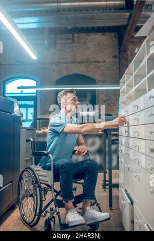 Profile of man in wheelchair touching in handle of drawer Stock Photo ...