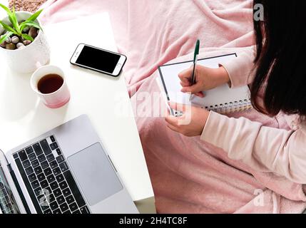 Woman covering pink blanket sitting on sofa holding a cup of tea with ...