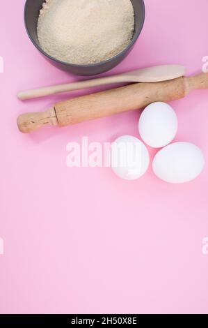 dark stoneware bowl with flour wooden rolling pin and white eggs on a pink background Stock ...