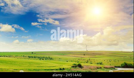 Hilly green field, windmill and sun on blue sky background ...
