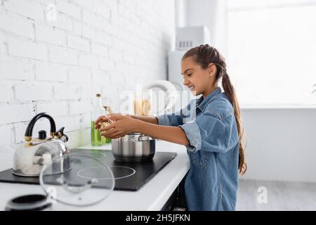 Smiling child holding macaroni near saucepan and looking at camera in kitchen Stock Photo - Alamy