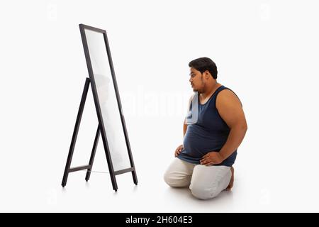 Portrait of a fat man looking at bellyfat in mirror with surprise ...