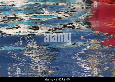 Shapes and colours in reflections of fishing boats in water of harbour ...