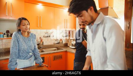 Three Indian friends talking while preparing dinner in the kitchen ...