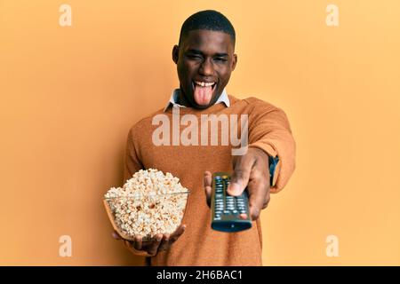 Young man eating popcorn sticking tongue out happy with funny ...