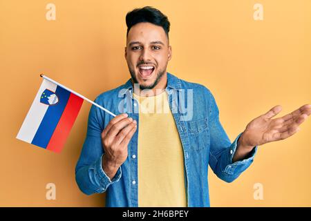 Young arab man holding slovenia flag smiling happy pointing with hand ...