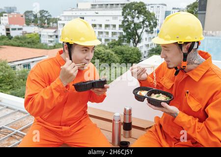 Hungry construction workers sitting on steps and eating sandwiches with ...