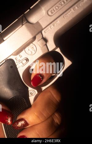 Lady spy detective with painted red nail varnish holding pistol gun at ...
