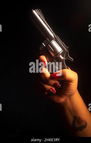 Lady spy detective with painted red nail varnish holding pistol gun at ...