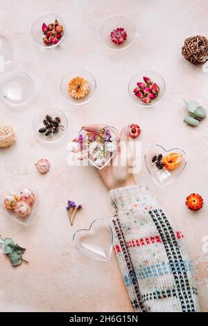 Woman filling heart shape ornament with dried flowers on beige concrete ...