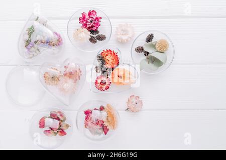 DIY ornaments filled with dried flowers on white wooden background with ...