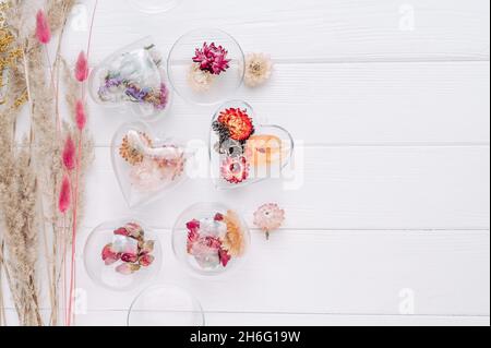 DIY ornaments filled with dried flowers on white wooden background with ...