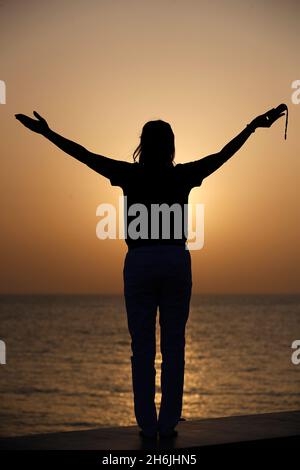Silhouette of faithful woman praying with rosary beads at sunset ...