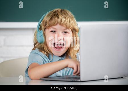 Clever excited school boy, amazed pupil wears headphones writing on ...