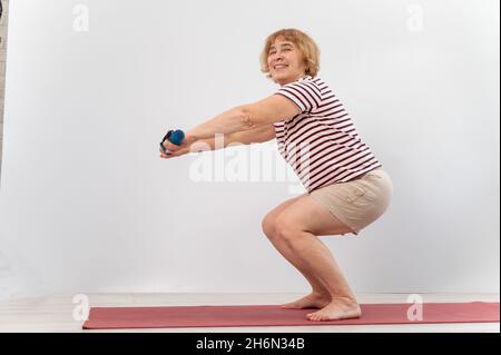 Elderly woman doing squats on a white background. The old lady is doing ...