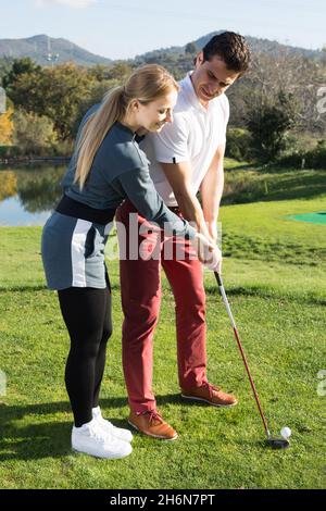 Female trainer of golf helping a young man to master the skills of the ...