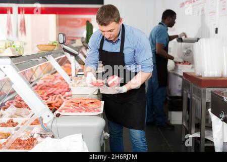 Two butchers arranging meat display Stock Photo - Alamy