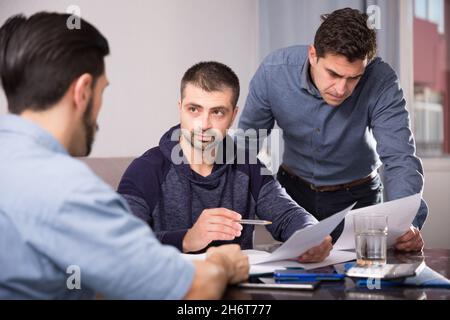Three upset males with papers at table Stock Photo - Alamy