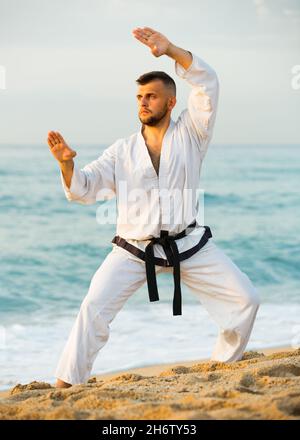 Sportsman is training the Shiko-dachi stance on the beach near the sea ...