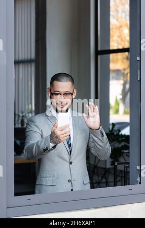 tattooed asian businessman smiling during phone conversation in office ...