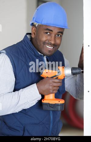 Young smiling guy using drilling machine to make drawer at workshop ...