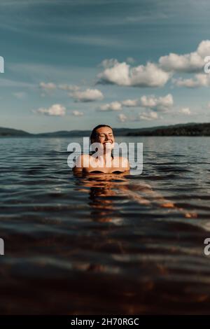 Smiling woman relaxing in an outdoor hot tub and raising a glass of ...
