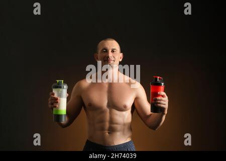 Male bodybuilder with protein shakes on dark background, back view ...