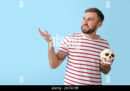 Handsome man showing human skull on blue background Stock Photo - Alamy