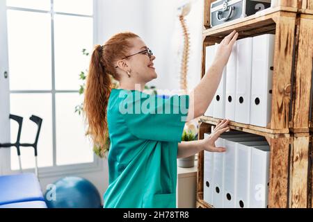 Young redhead woman wearing phsiologist uniform holding binder at ...