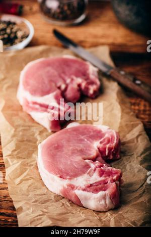 Two pork loin steaks on baking paper with lemon and peppercorn Stock ...