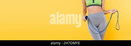 partial view of sportive woman with skipping rope isolated on yellow ...