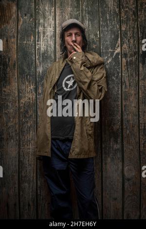 Junkie man with cap green anorak and blue sweatpants near wooden old ...